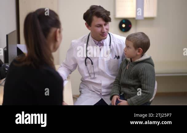Charming boy sitting on lap of smiling doctor answering questions with ...
