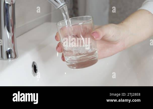 girl draws water into a transparent glass from a metal tap,female hand ...