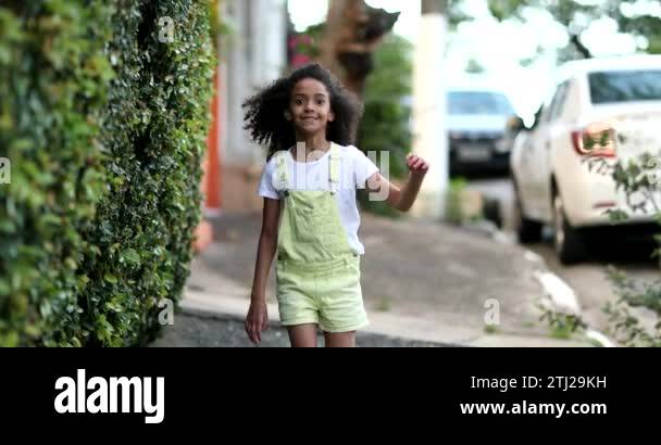 Happy little girl hopping outside in city sidewalk. Mixed race kid ...