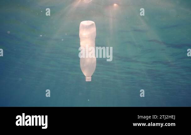 White plastic buttle drift under surface of water in sunrays. A plastic ...