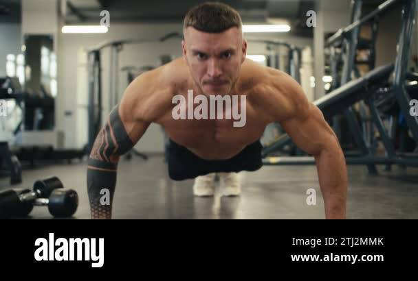 Strong athletic man trains shirtless in the gym, doing push-ups. Lean ...