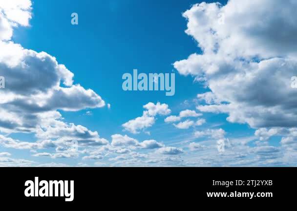 White fluffy clouds slowly float through the blue daytime sky timelapse ...