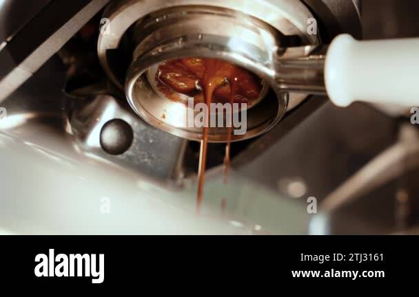A barista pours steaming hot coffee from a professional machine. The ...