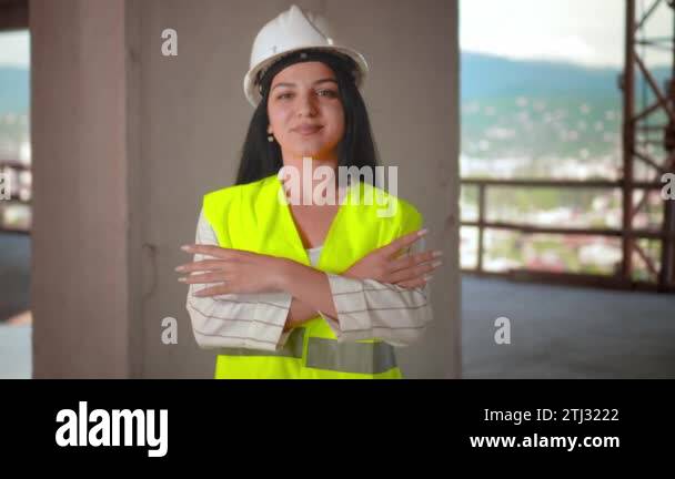 Middle-aged female architect wearing helmet and green vest crosses her ...