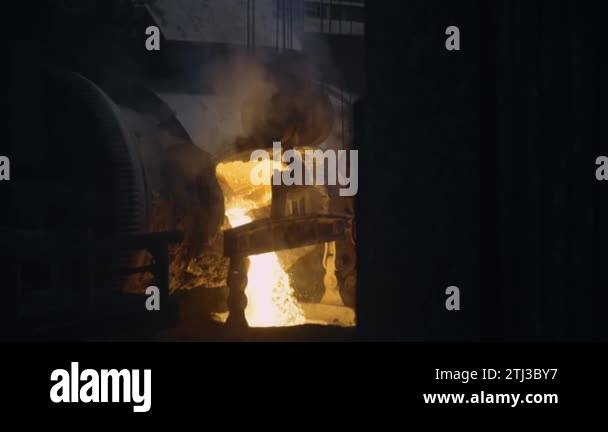 Molten metal flows from the furnace into the ladle. Sparks splatter ...