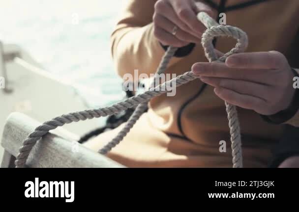A sailor on a catamaran shows how to tie a sea knot. Close-up of hands ...
