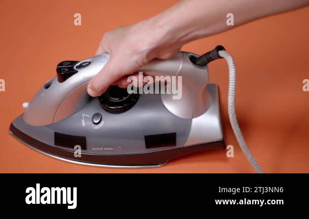 Female Hand Ironing a Bright Orange Cloth with a Steam Iron on an ...
