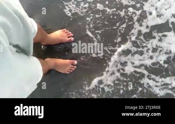 a tourist is standing on the beach and feeling the beach waves with his ...