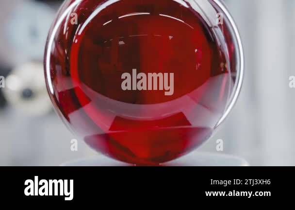 Red liquid boils in a round glass flask. Bright laboratory. Production ...