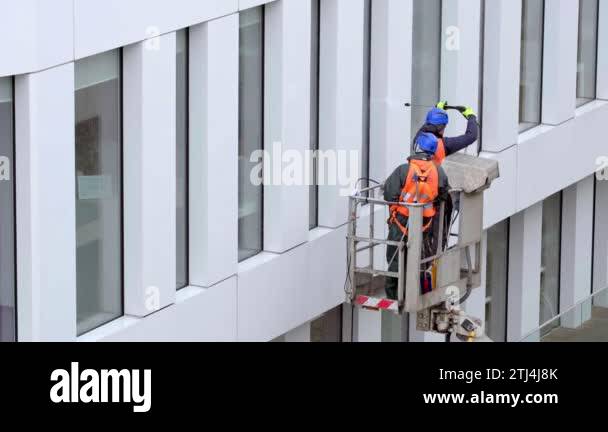 Two workers wearing safety harness wash walls, panels and windows of ...