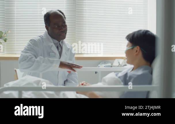 Zoom in shot of mature African American doctor sitting at bedside in ...