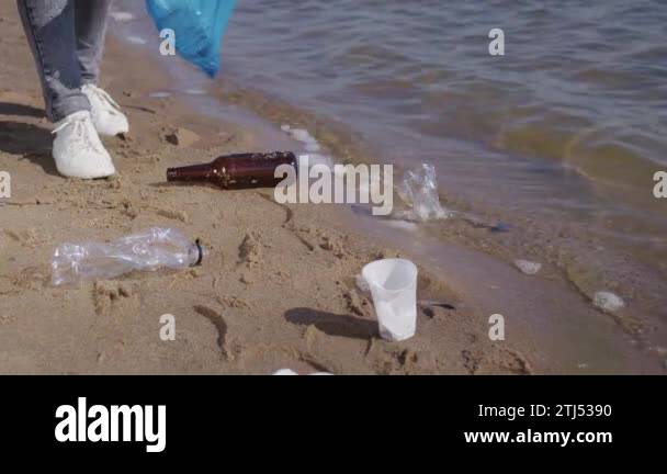 Woman picks up plastic bags and bottles scattered on wet sand of ...