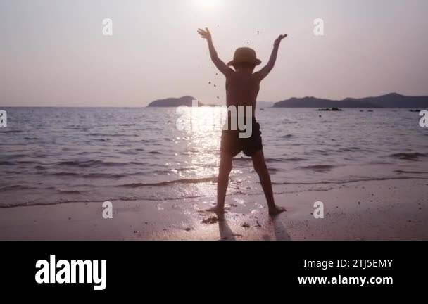 A video showing the back view of a boy throwing wet sand on the sea at ...