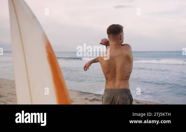 Rear view of young shirtless caucasian man in swimwear stretching by ...
