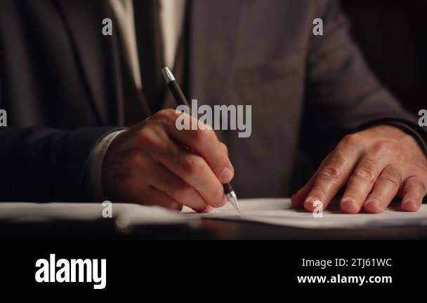 A man in a strict business suit sits at a table and writes something on ...