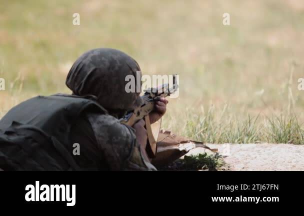 An army man in a green uniform vest is unloading a machine gun, lying ...