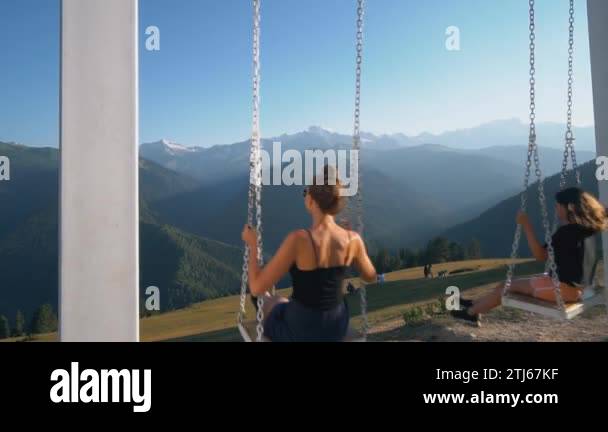 Young woman rides swing over cliff on slope, in front of her background ...