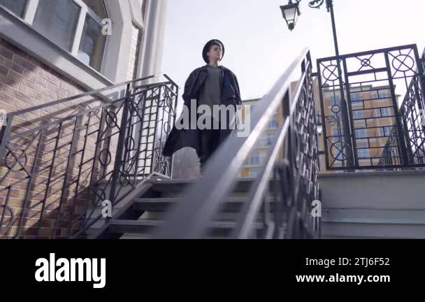 Young gorgeous woman in high-heels and hat standing upstairs with wind ...
