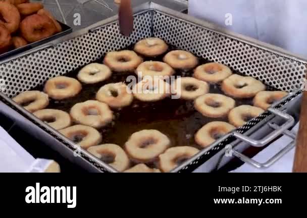 Fresh donuts in deep fat fryer at local food market. Process of junk ...