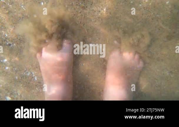 Woman standing barefoot on sand underwater and digging her feet into ...