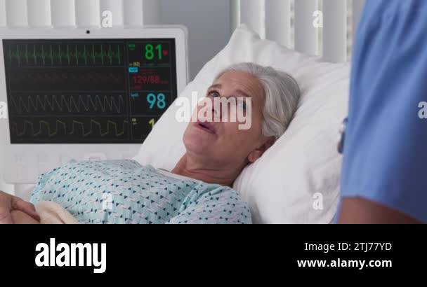 Ill elderly woman resting in hospital bed hooked up to ECG monitor ...