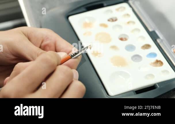 Dental technician coloring dental prosthesis with a paint brush at the ...