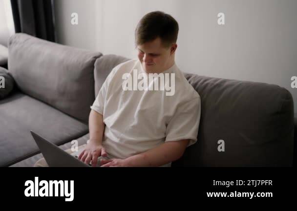 Man with down syndrome at home sits on sofa, typing on laptop Stock ...