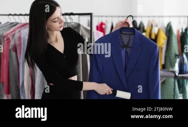Dry cleaning brunette worker removes pellets from woolen coat standing ...