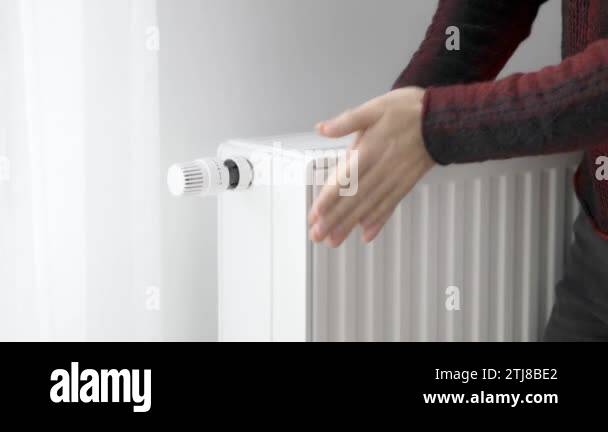 A man touches the cold radiator of a home heater with his frozen hands ...