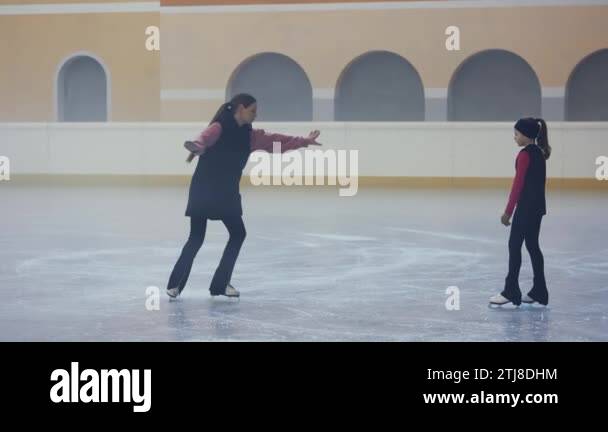 A professional woman figure skating coach demonstrates to her student ...