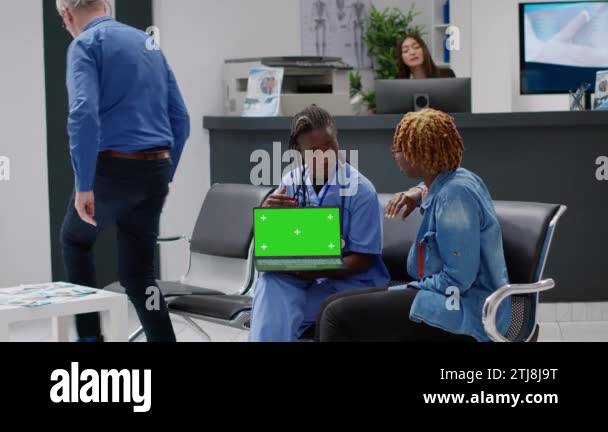 Nurse and patient looking at greenscreen display on laptop, sitting in ...