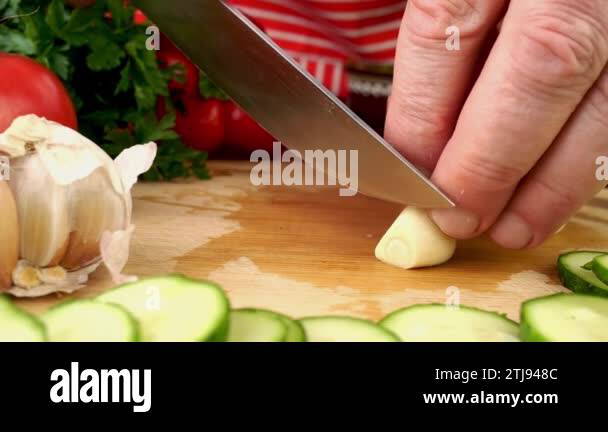 Slicing garlic with sharp knife on wooden cutting board on domestic ...