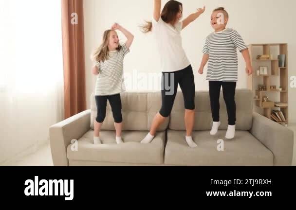 Mom and daughter and son of school age are dancing on the couch, they ...