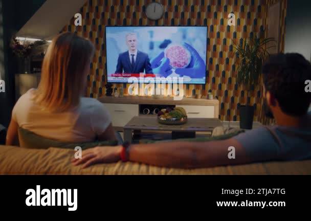 Couple sitting on couch, watching scientific TV news channel about ...