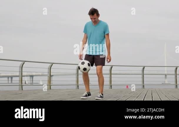 Man soccer player juggling a ball performing tricks on waterfront in ...