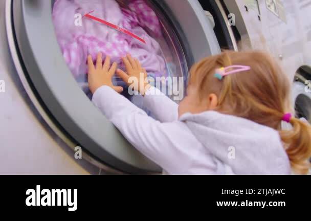 Little girl regular housekeeping work out towels into washing machine ...