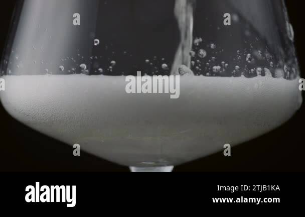 Golden fizzy beverage bubbling pouring into glass goblet in super slow motion close up. Bubbles ...