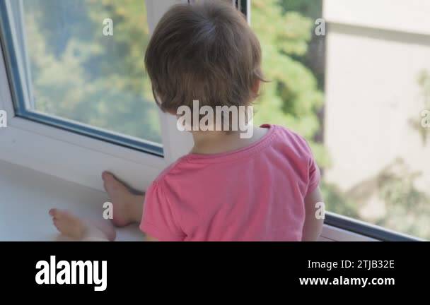 A small child sits on the windowsill and looks out the window at the ...