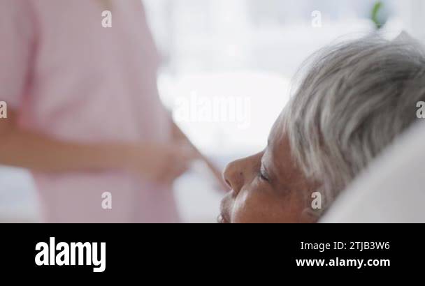 Diverse female doctor filling drip bag of senior female patient asleep ...