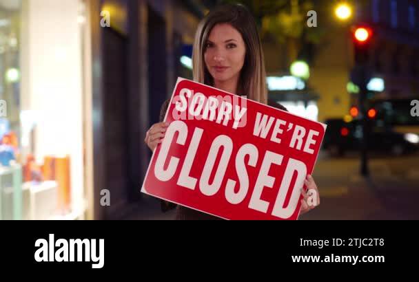 Woman holding Closed sign outside her small shop in the city at night ...