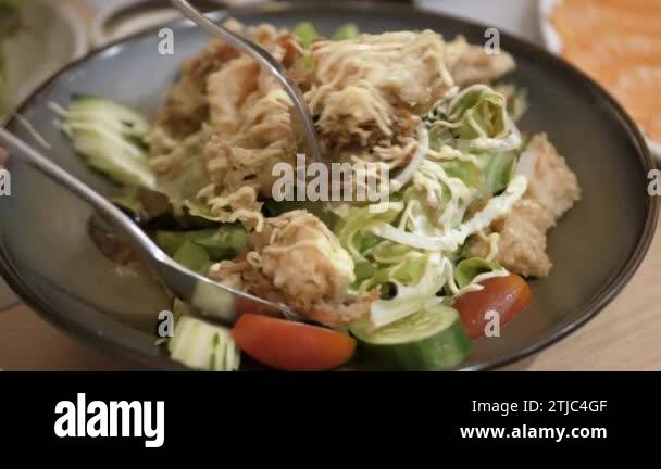 using fork and spoon helping to pick salad in a bowl full with ...