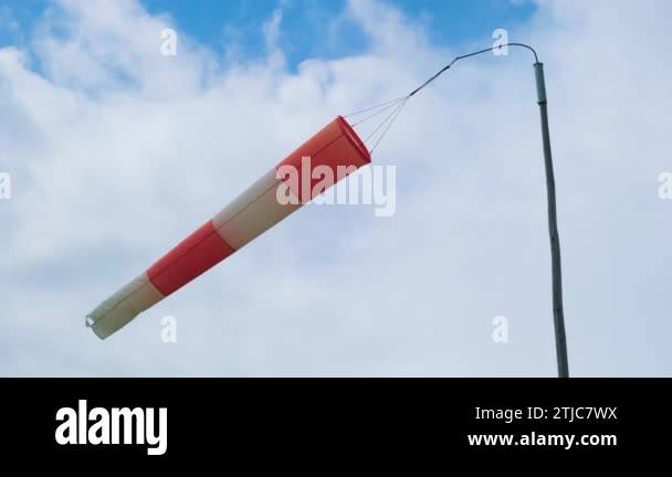 Red and white striped airport windsock on mast inflates in wind against ...