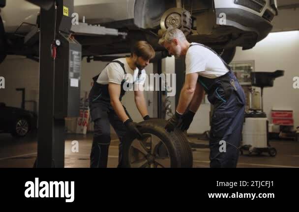Two men install a car wheel during a tire fitting. Fellow mechanics ...