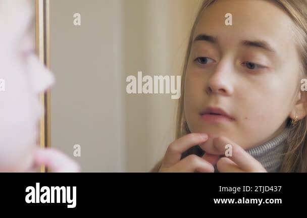 Portrait of a teenager girl who examines with concern in the mirror a ...