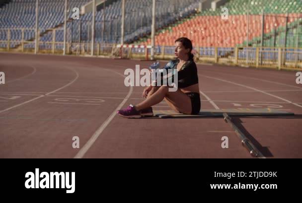 Full body handheld shot of young tired female sprinter in activewear ...
