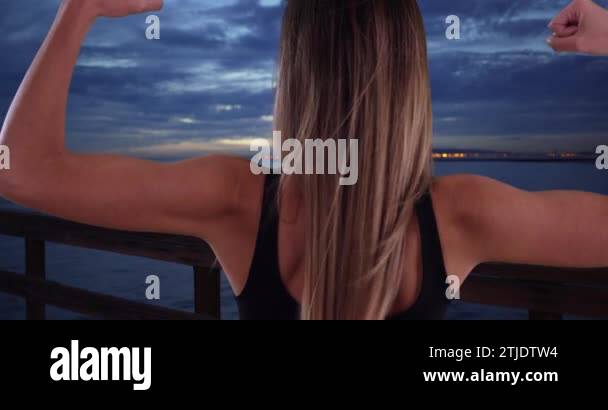 Rear view of athletic woman flexing and kissing biceps standing ...