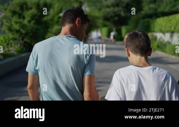 Back of father walking with teen son in beautiful green park. Parent ...
