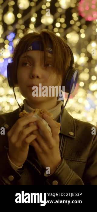 Vertical front view of a teenage girl eating hamburger and listening to ...