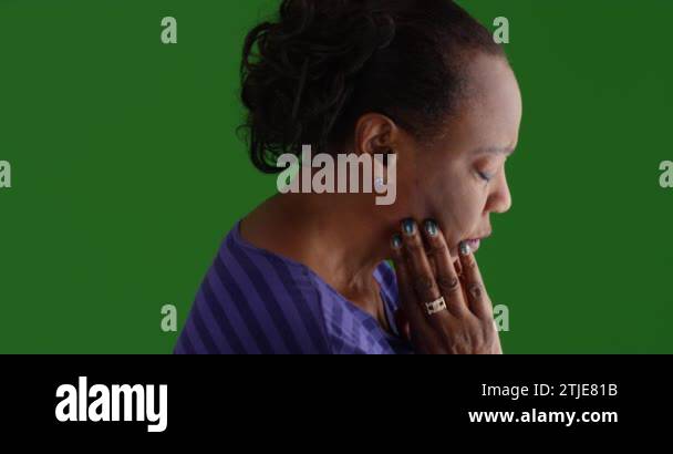 An older black woman mournfully looks out her window on green screen ...