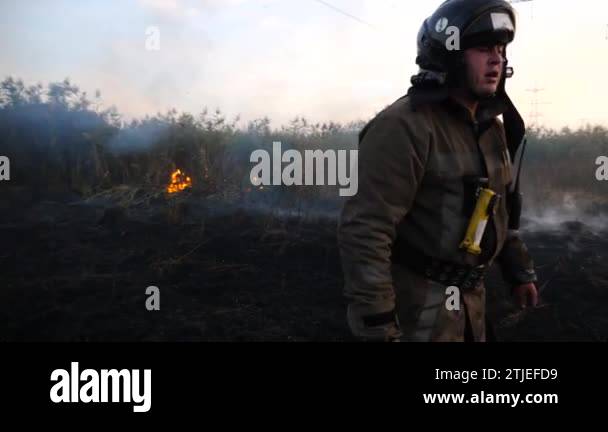 Young fireman in uniform going on burnt grass at countryside. Male ...